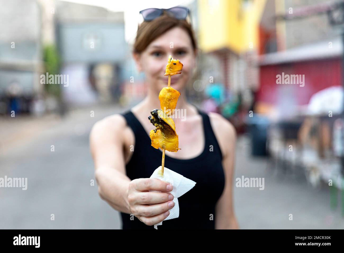 Tourist woman trying seafood on a stick grilled on a food stall in in ...