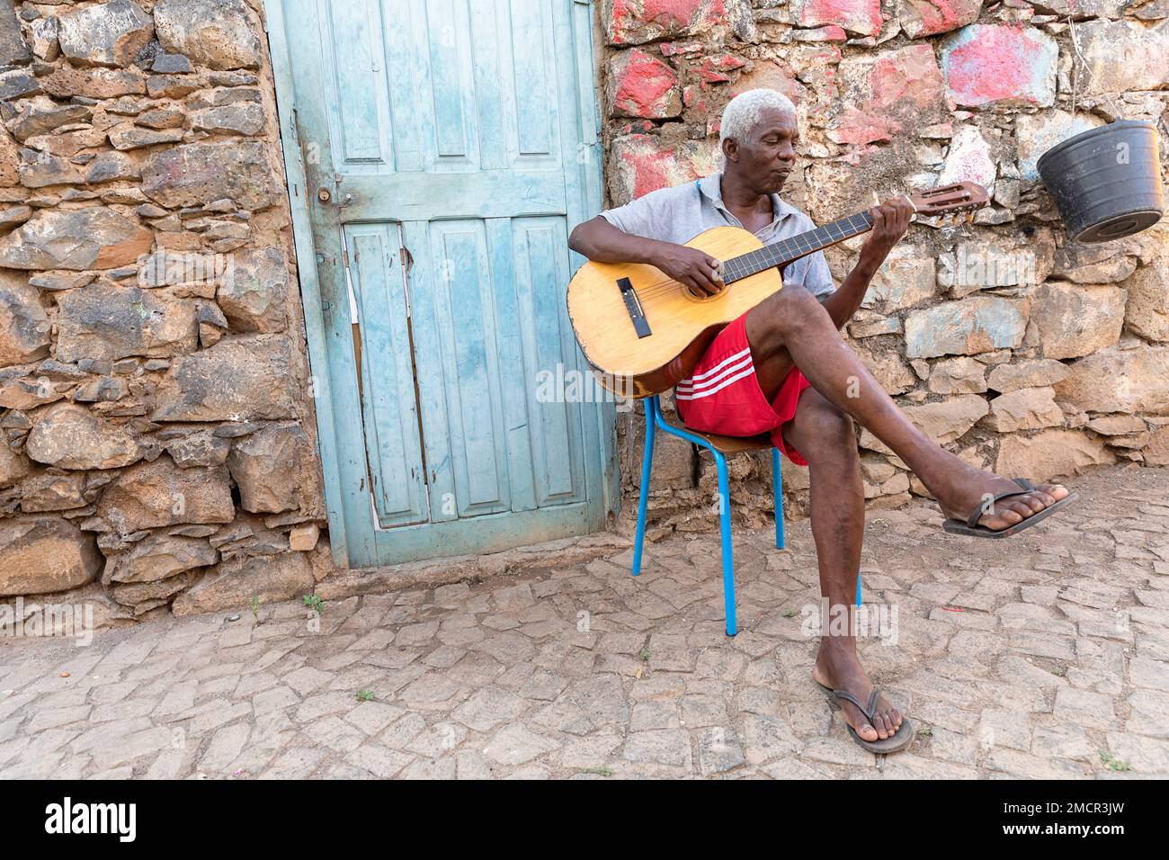 Local men sitting infront of the entrance to his house, playing guitar ...
