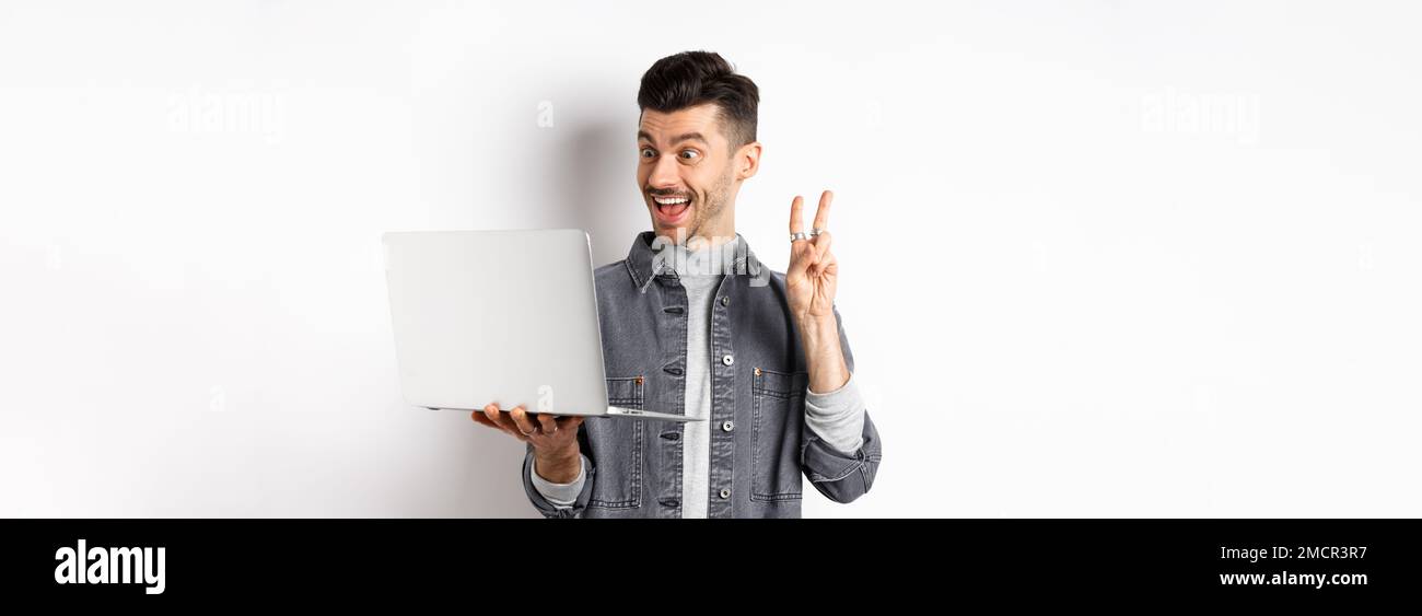 Funny young man video chat on laptop, showing v-sign and smiling at ...
