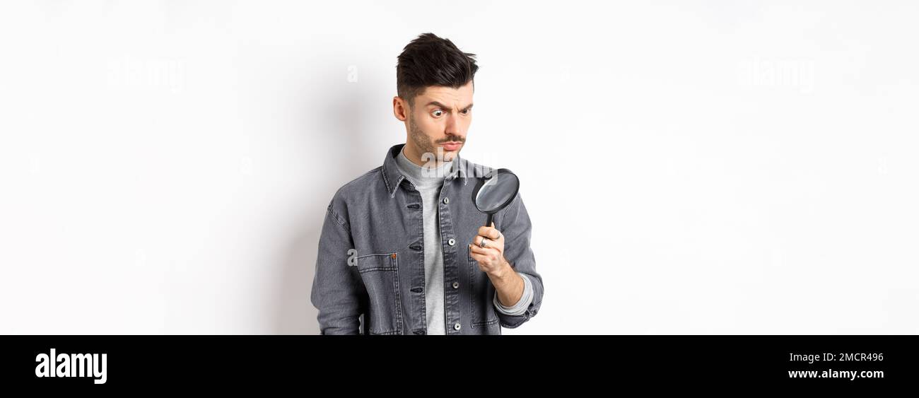 Serious man investigating, looking down with magnifying glass, stare ...