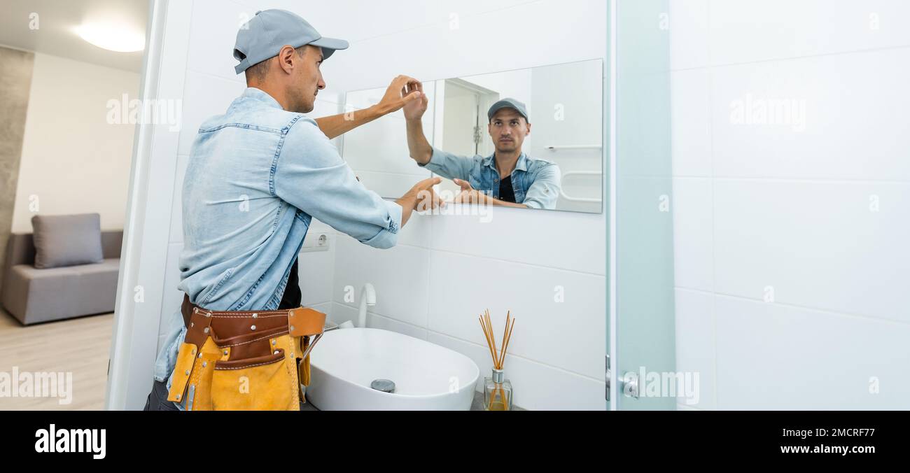 Handyman installing mirror in bathroom Stock Photo - Alamy
