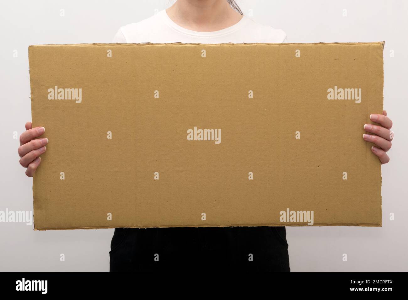 A woman's hands hold a blank cardboard sign, wear a white t-shirt and ...