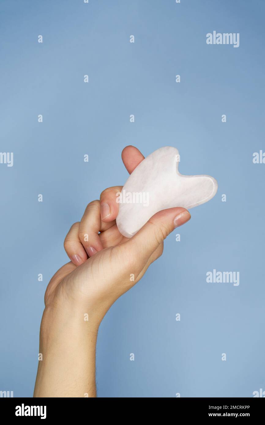 Female hands with gua sha massage stone scraper tool on blue background ...