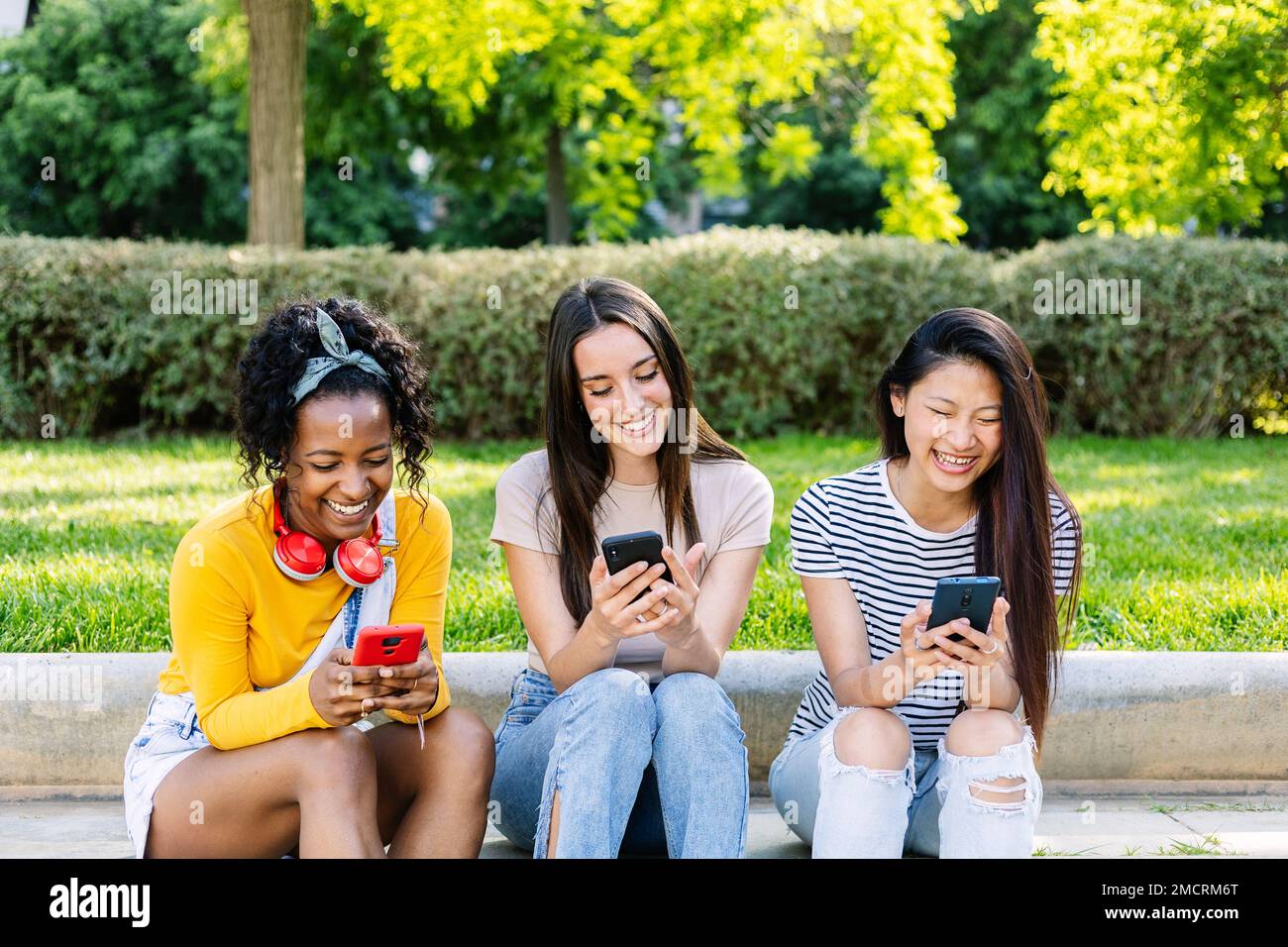 Teenage woman friends using mobile phone together sitting outdoors Stock Photo - Alamy
