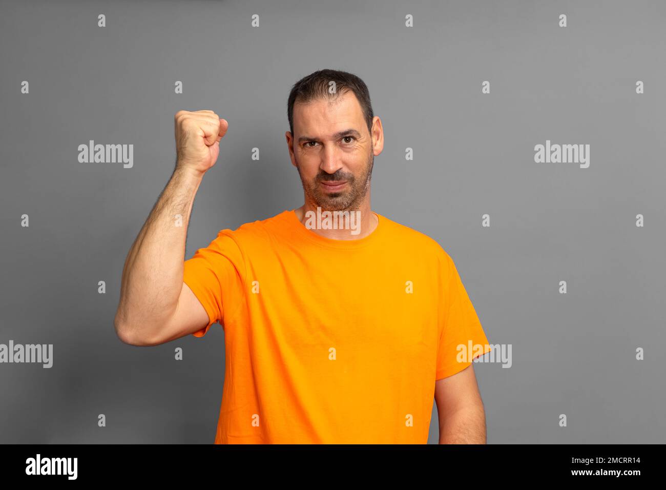 Bearded hispanic man wearing an orange t-shirt celebrating something ...