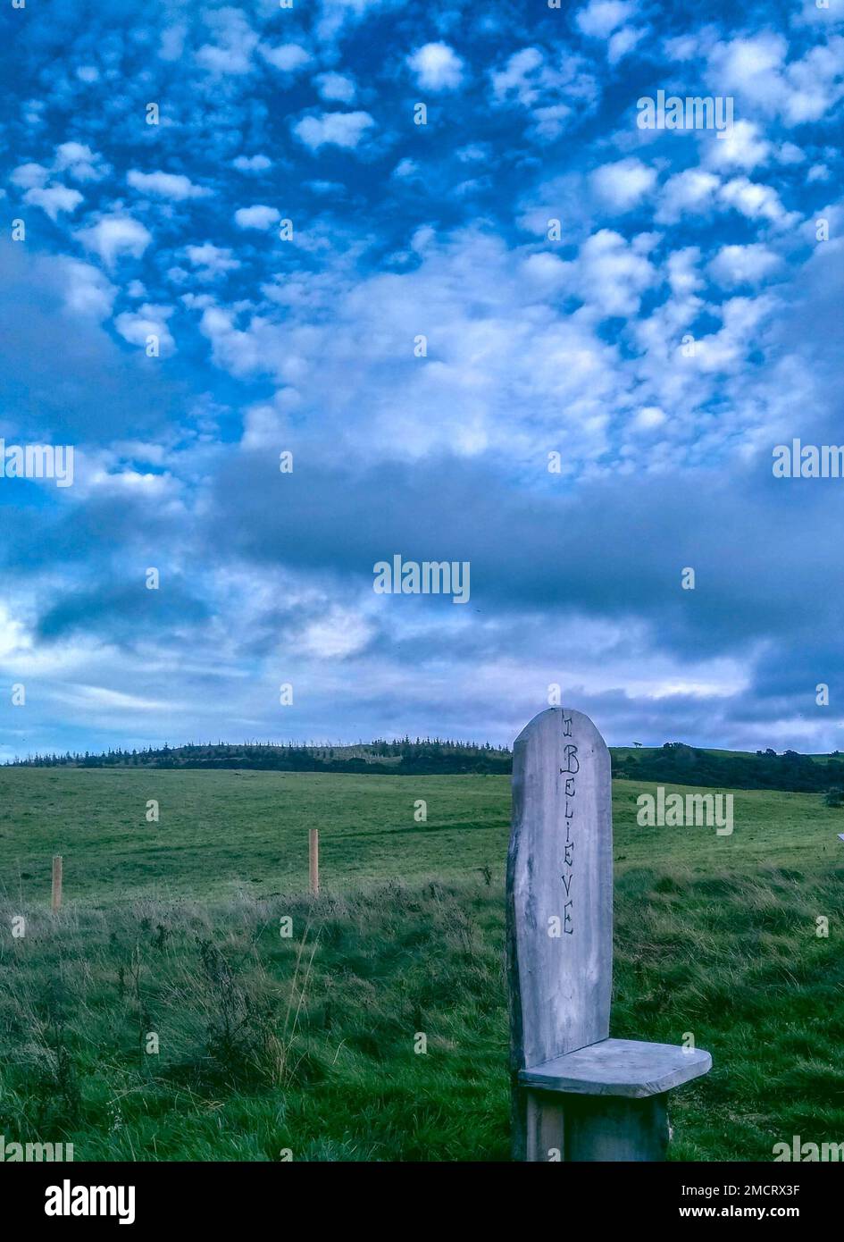 A vertical shot of a stone chair in a field under a blue sky with ...