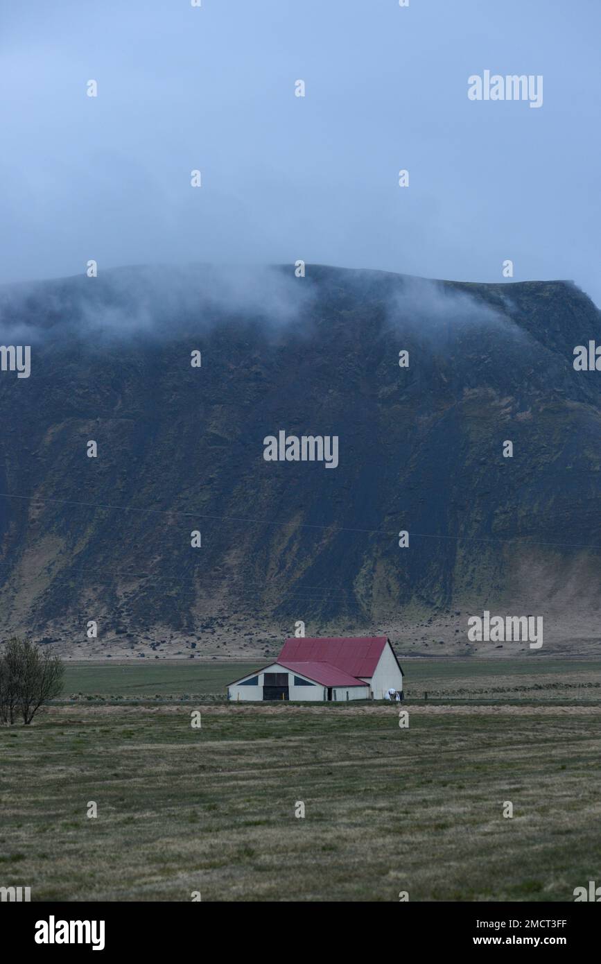 Misty morning in Iceland with a red roofed house below a mountain with ...