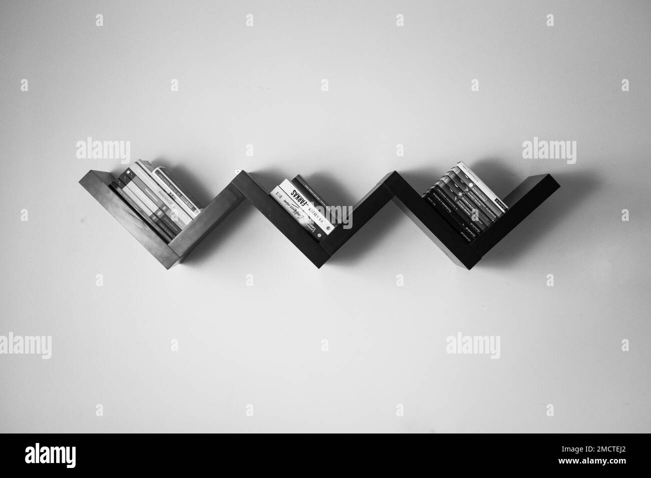 A grayscale of a small and compact w-shaped bookshelf mounted on a wall ...