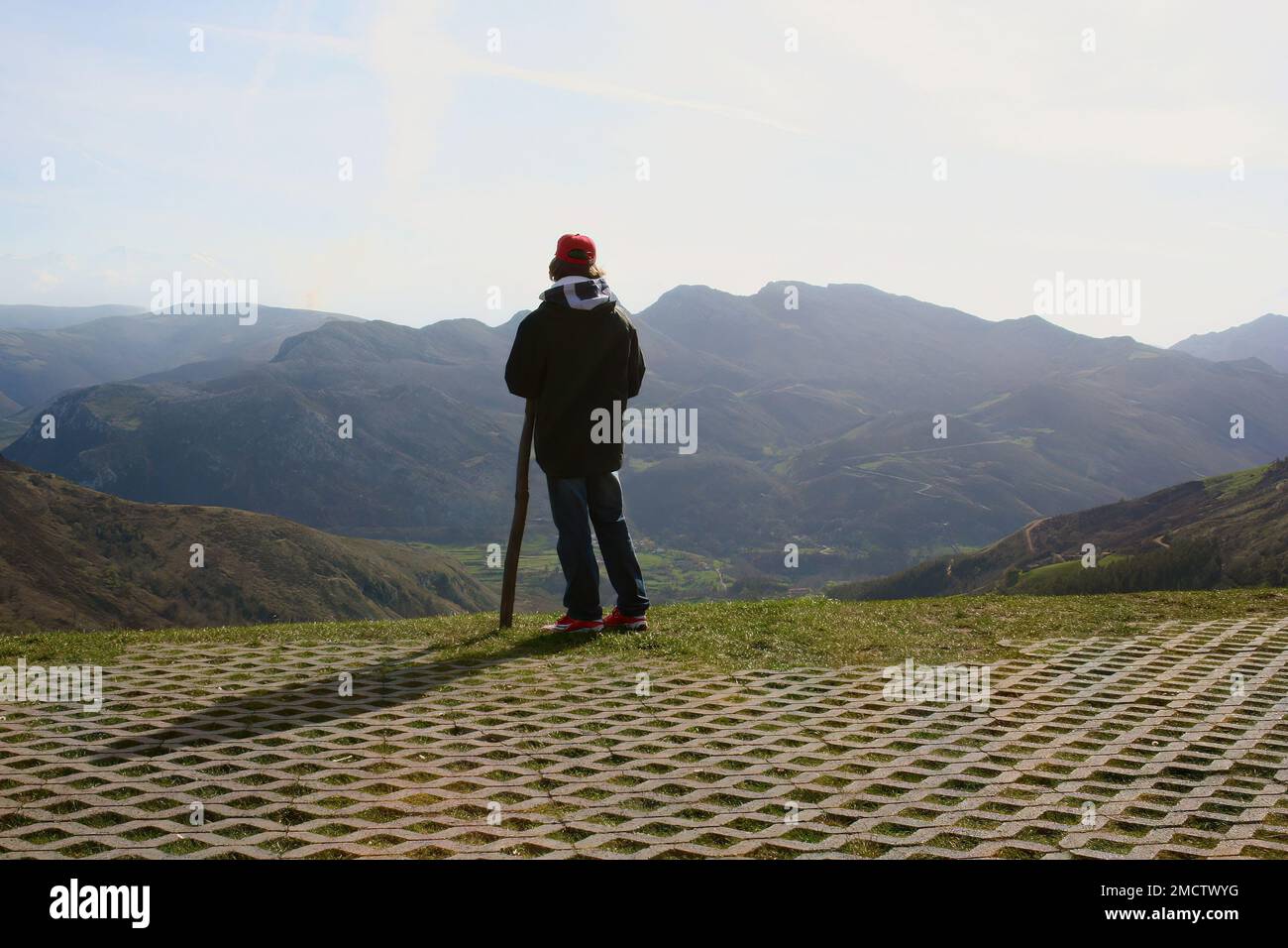 Vast landscape with mountain peaks and teenage boy with a stick ...
