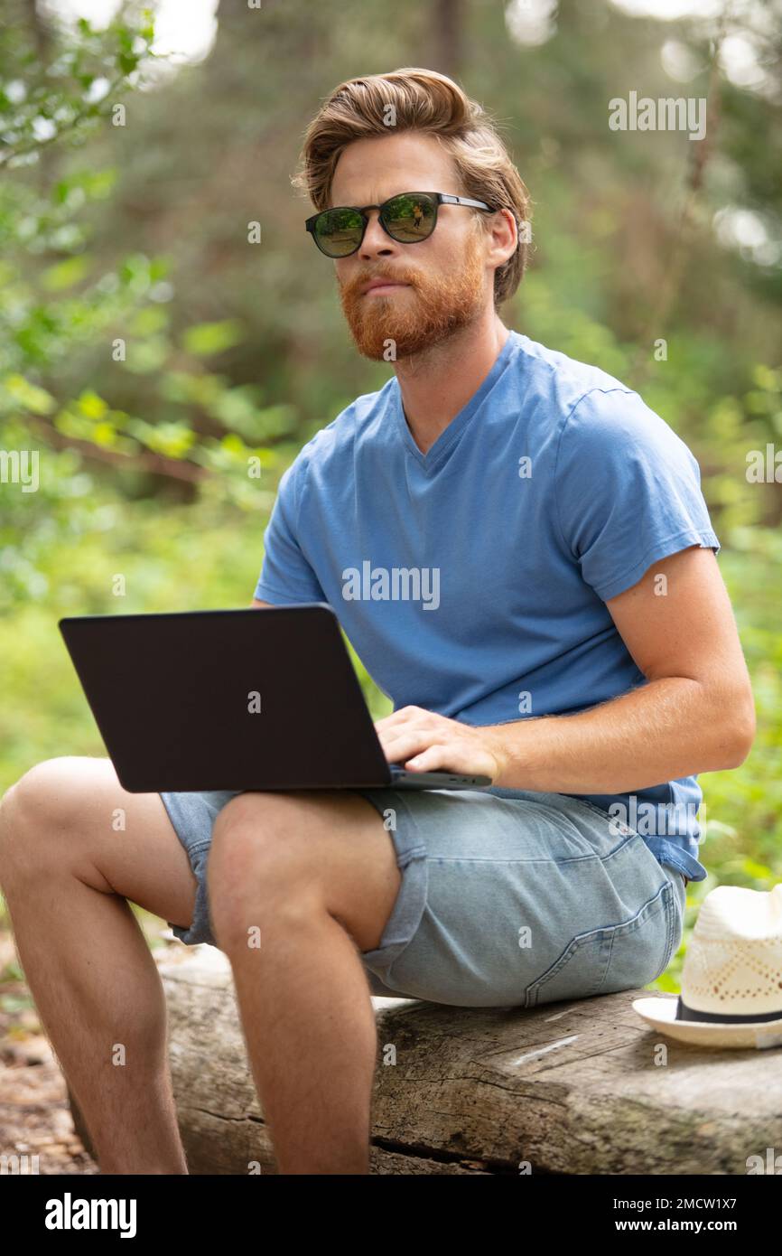 man sits on tree trunk in forest using laptop computer Stock Photo - Alamy