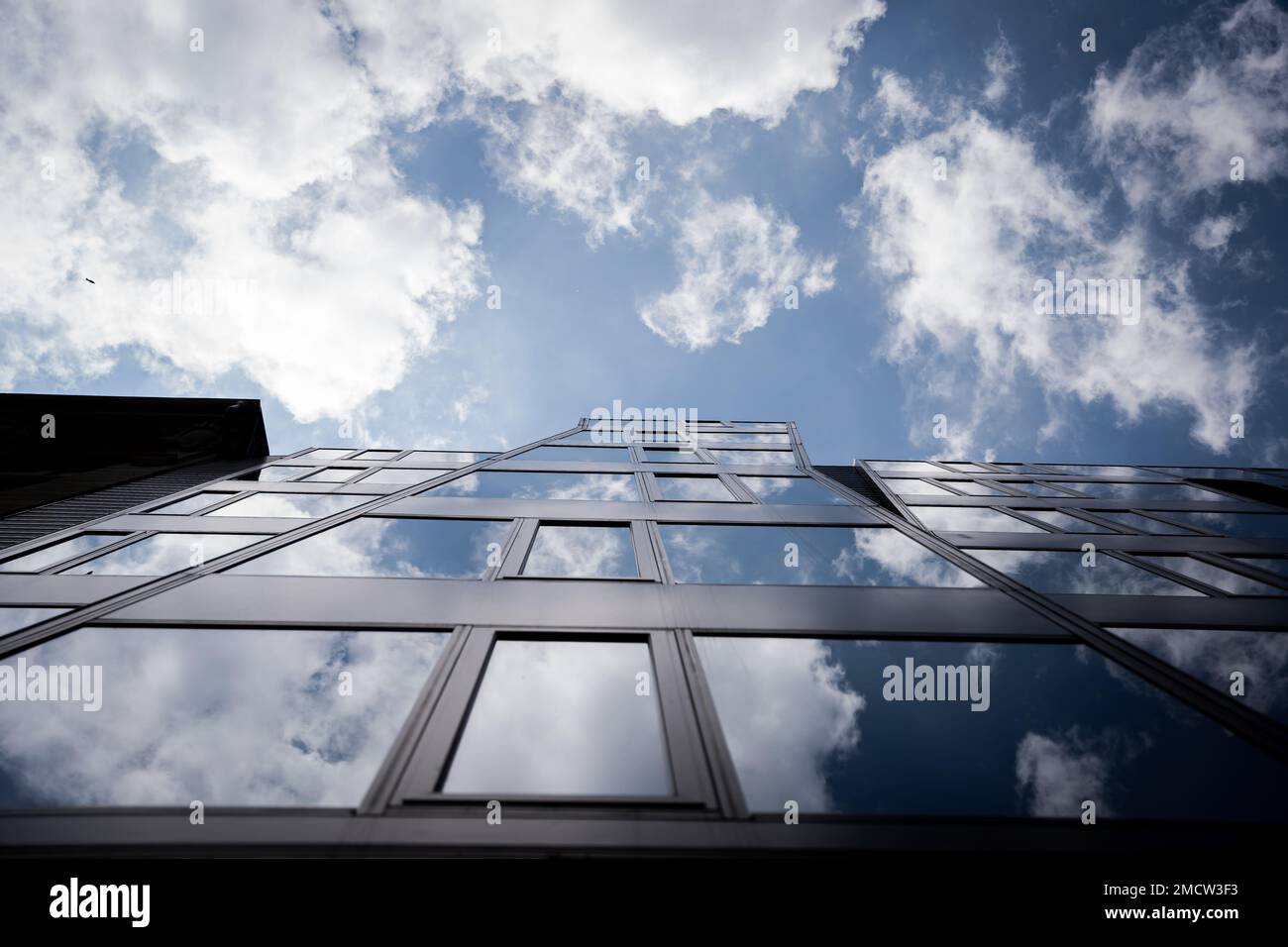 A low angle of a modern glass-walled building with a reflection of sky ...