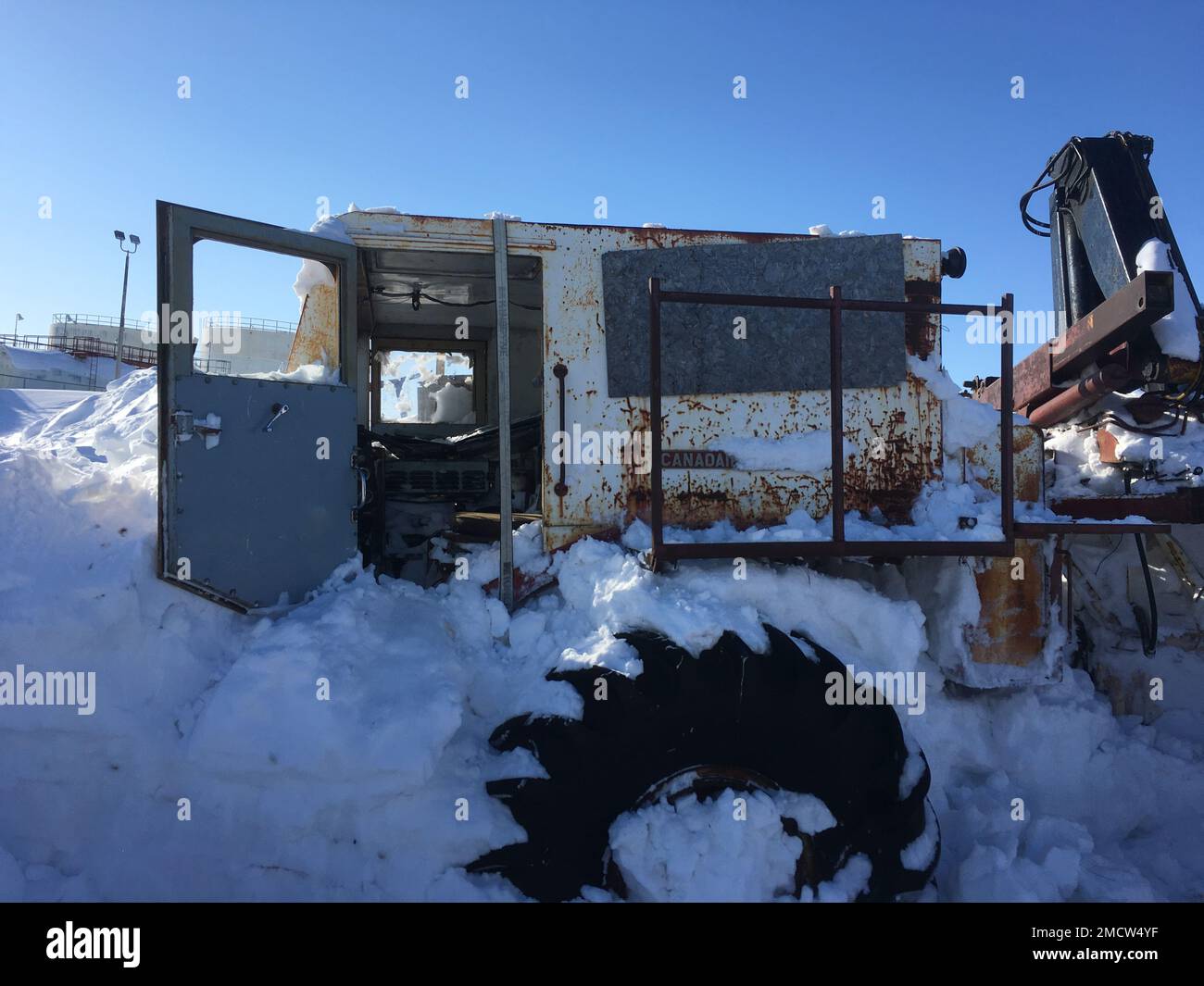 An abandoned, wrecked tractor buried in snow under the blue sky in the ...