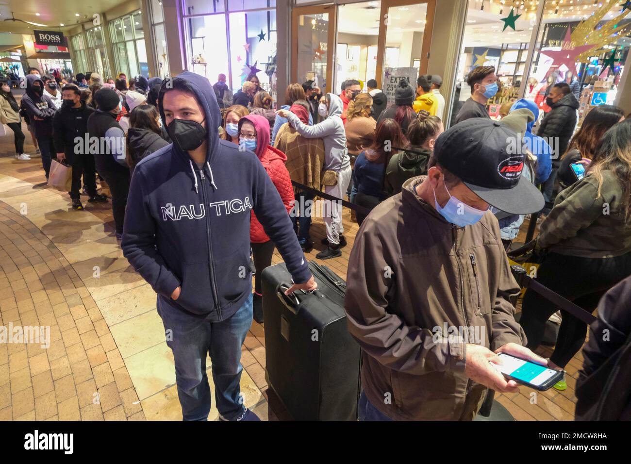 Black Friday shoppers wearing face masks wait in line to enter a store ...