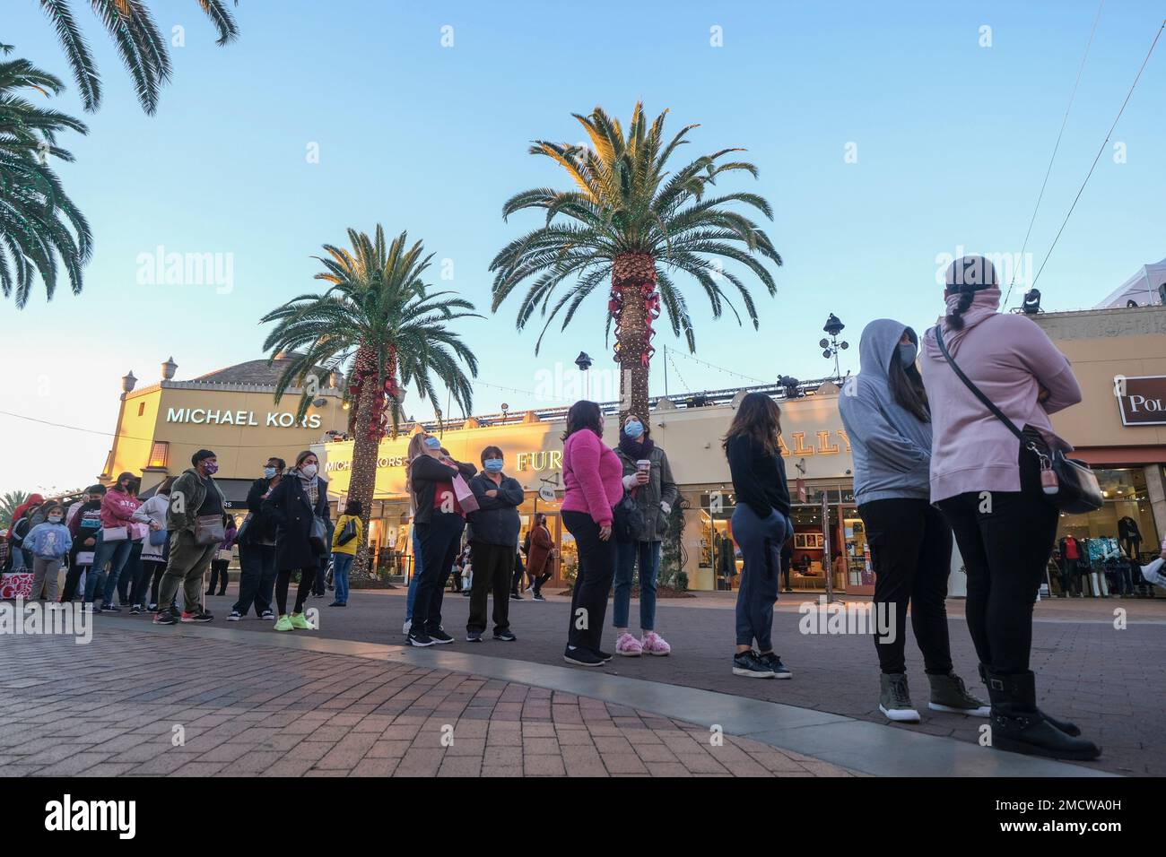 Black Friday shoppers wearing face masks wait in line to enter a store ...