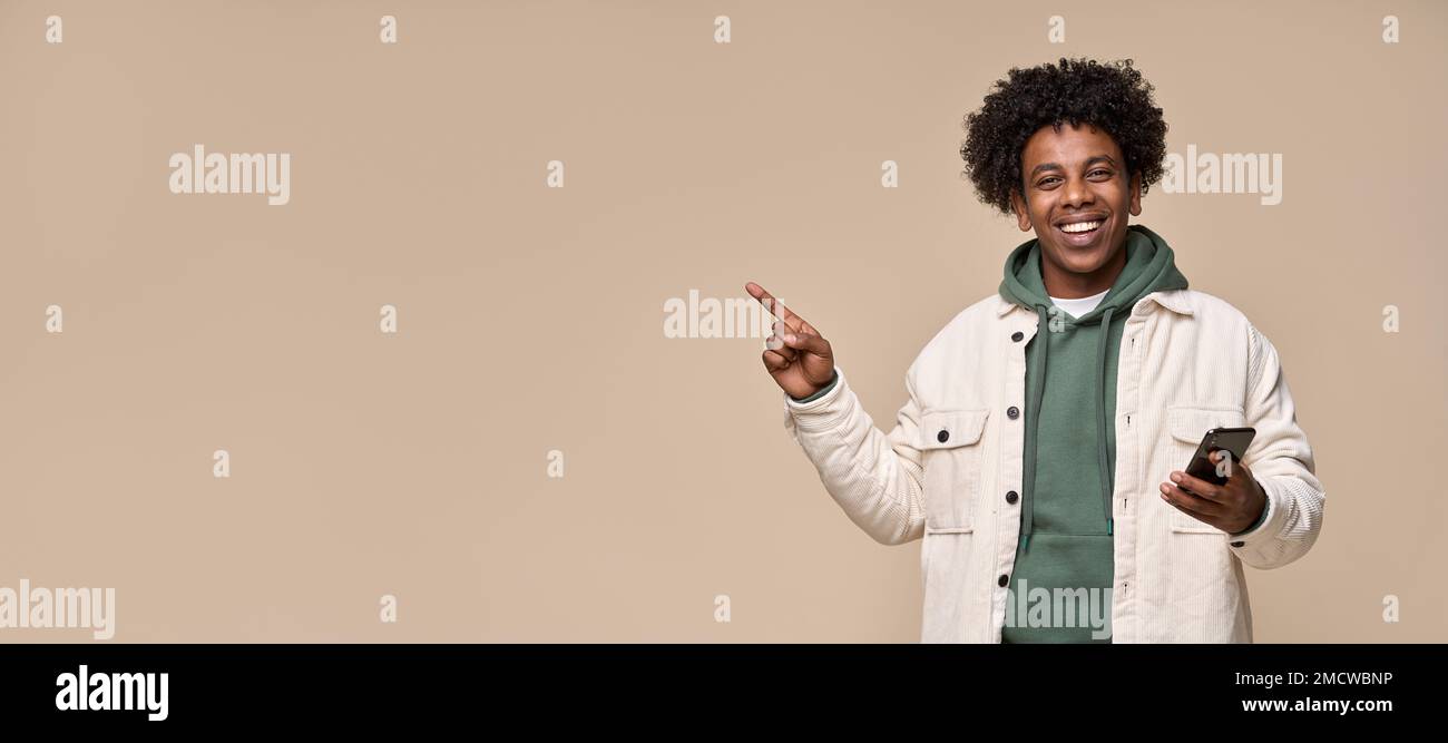 Happy African gen z guy holding mobile phone pointing finger ...