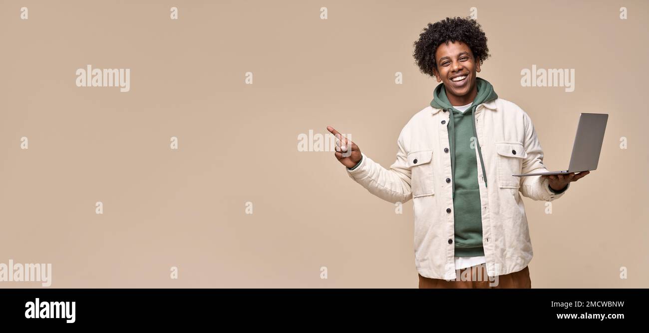 Happy African student holding laptop pointing at copy space isolated on ...