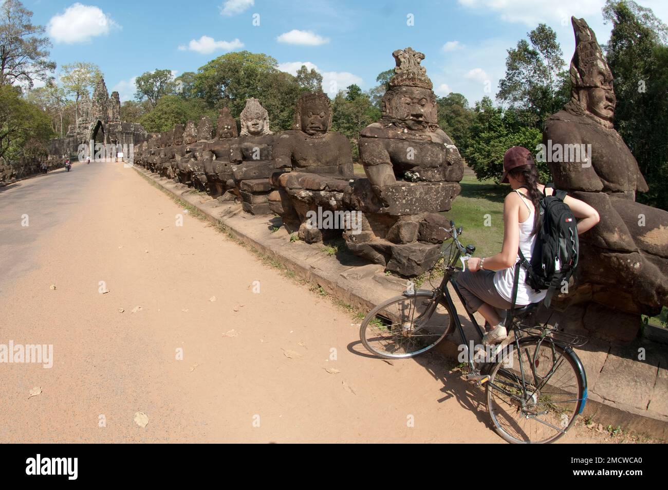 Tourist on bike on road with sculptures of Asuras (demonic monsters) to ...