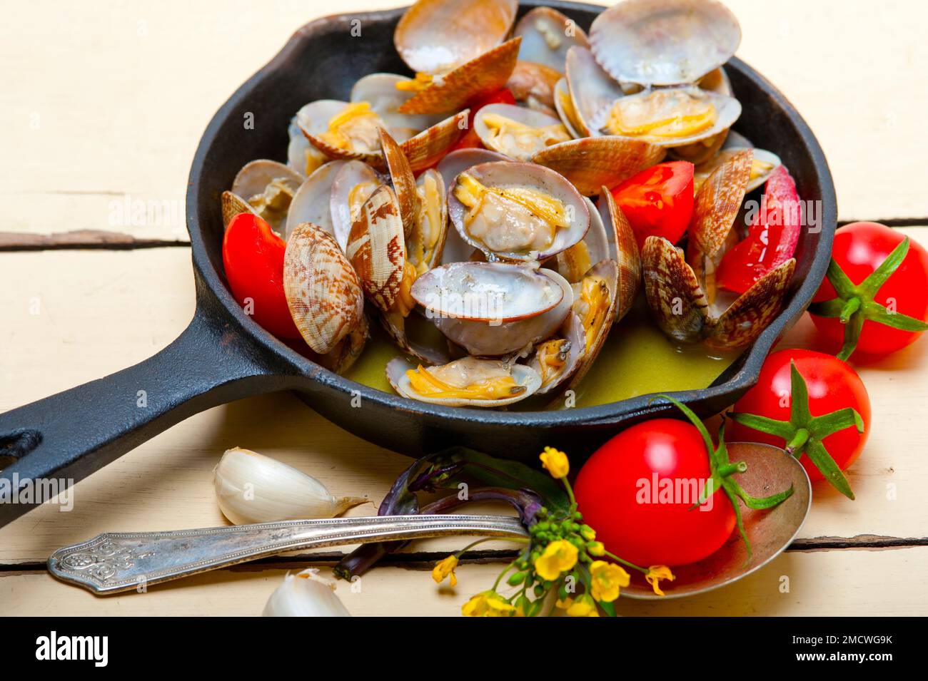 Fresh clams stewed on an iron skillet over wite rustic wood table Stock ...