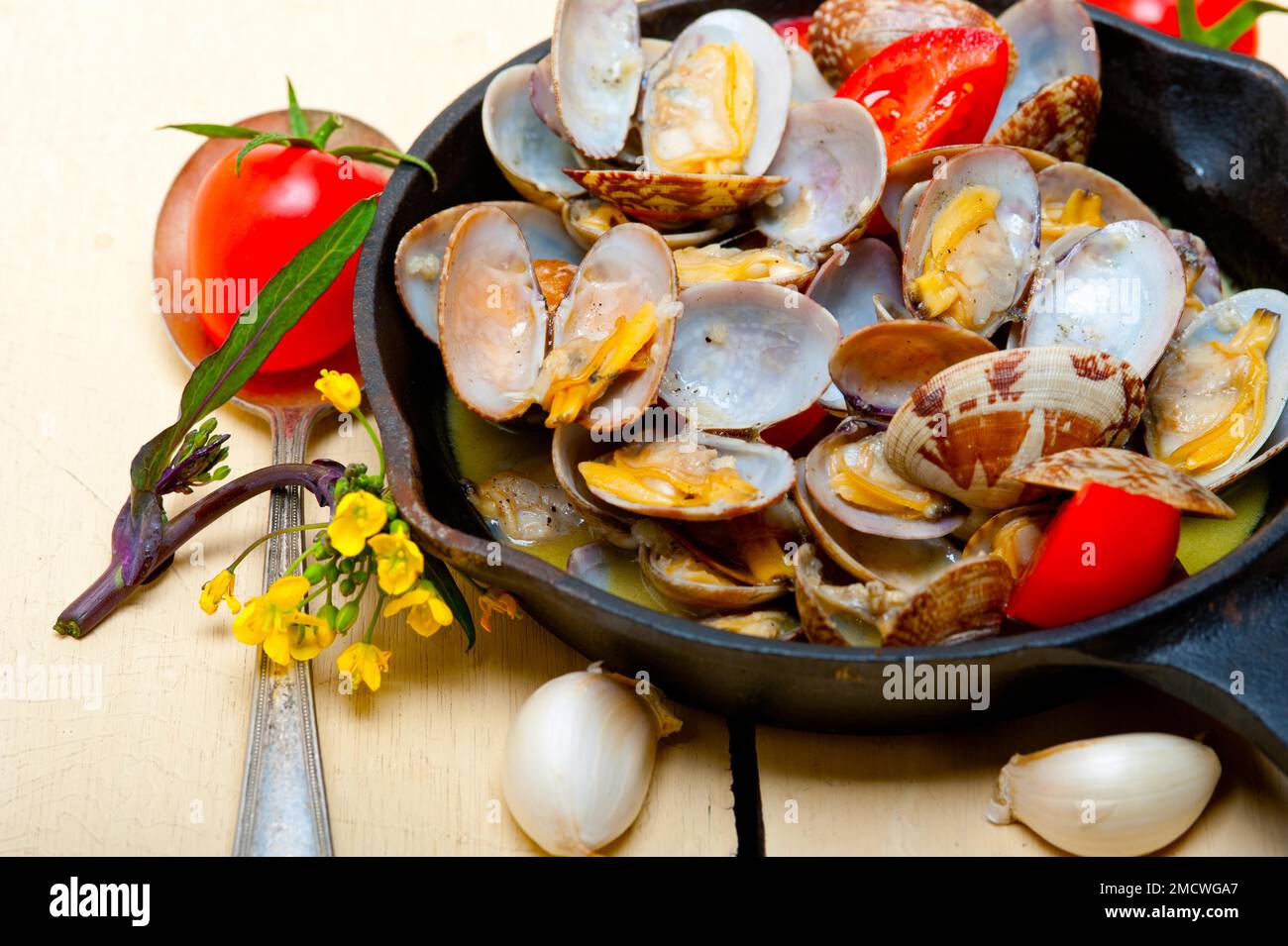 Fresh clams stewed on an iron skillet over wite rustic wood table Stock ...