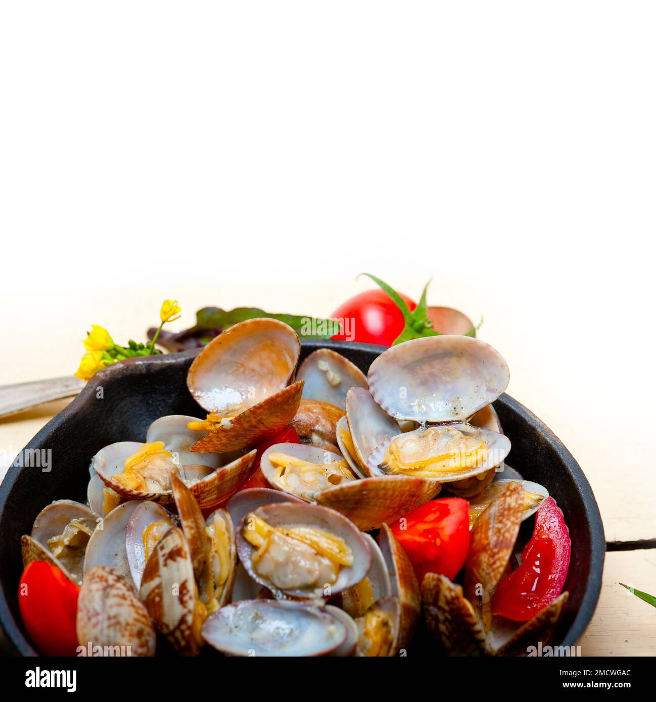 Fresh clams stewed on an iron skillet over wite rustic wood table Stock ...