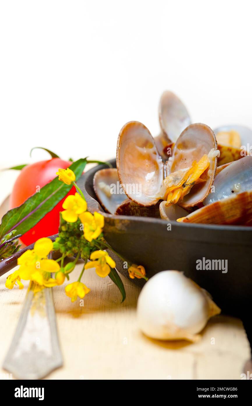 Fresh clams stewed on an iron skillet over wite rustic wood table Stock ...