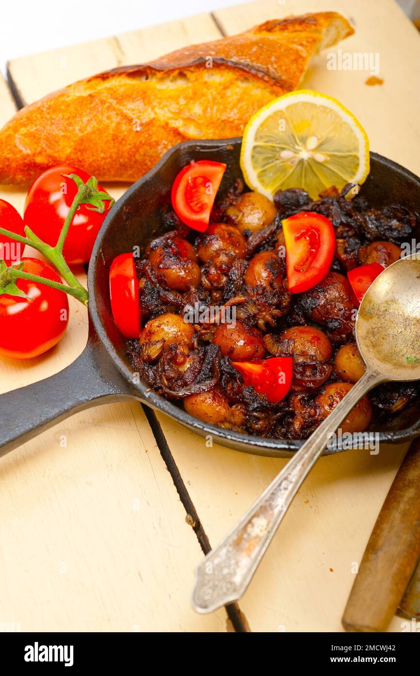 Baby cuttle fish roasted on iron skillet with tomatoes and onions over ...