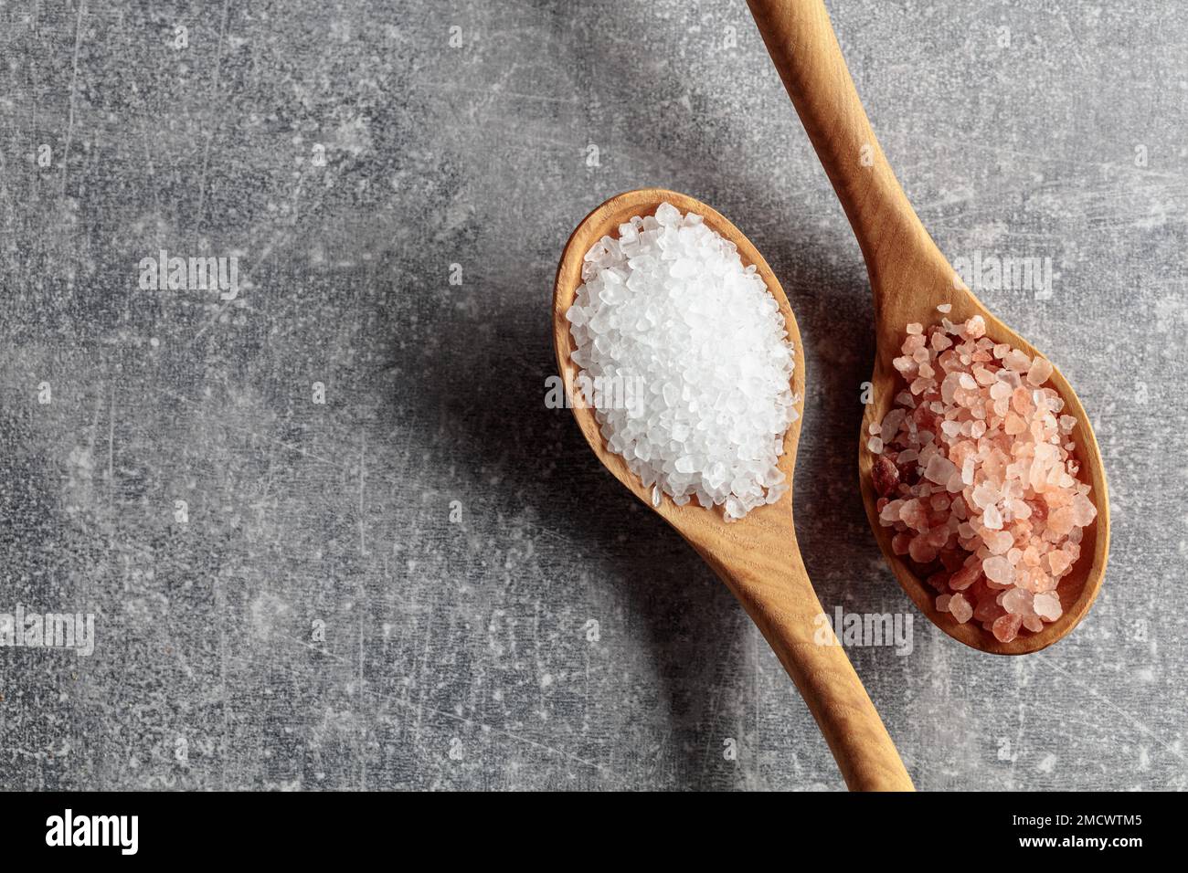 Pink and sea salt in wooden spoons on a grey stone background. Copy ...
