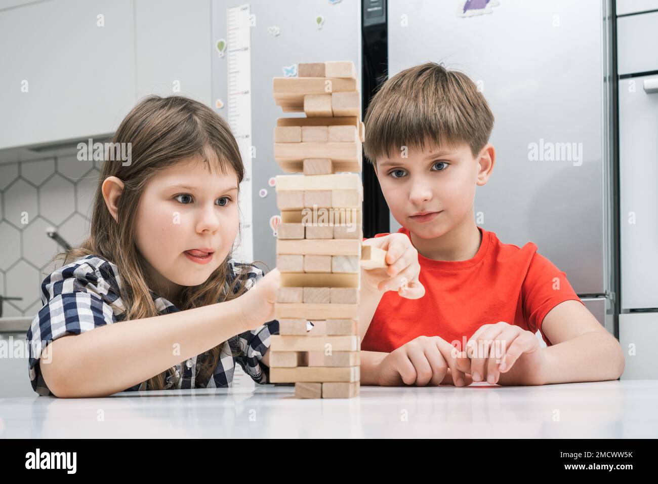 Two children playing board game Jenga on table in kitchen at home ...