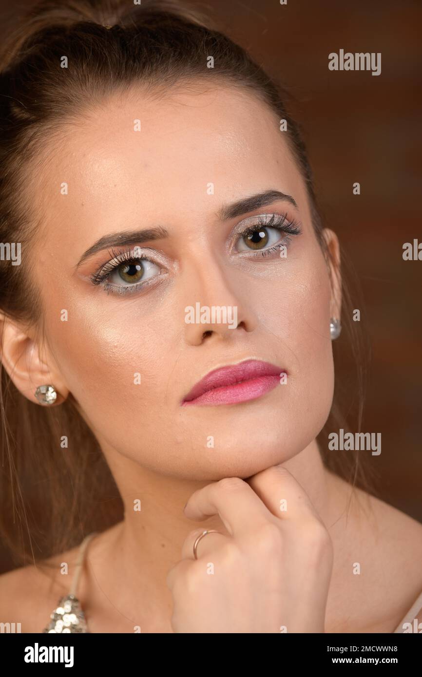 Pretty young woman with long hair and discreet make-up against a brown ...