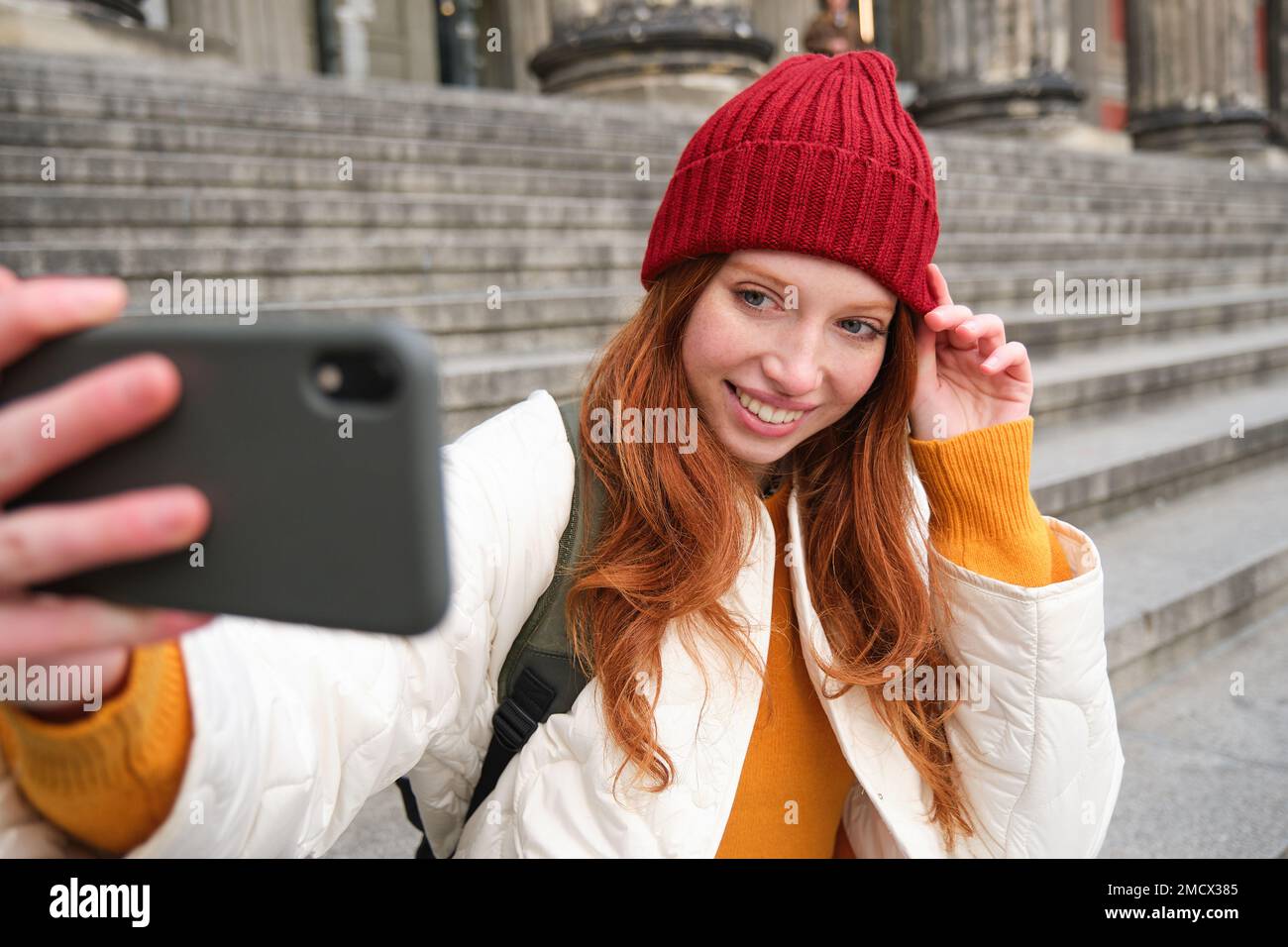 Stylish young girl in red hat, takes photos on smartphone camera, makes ...