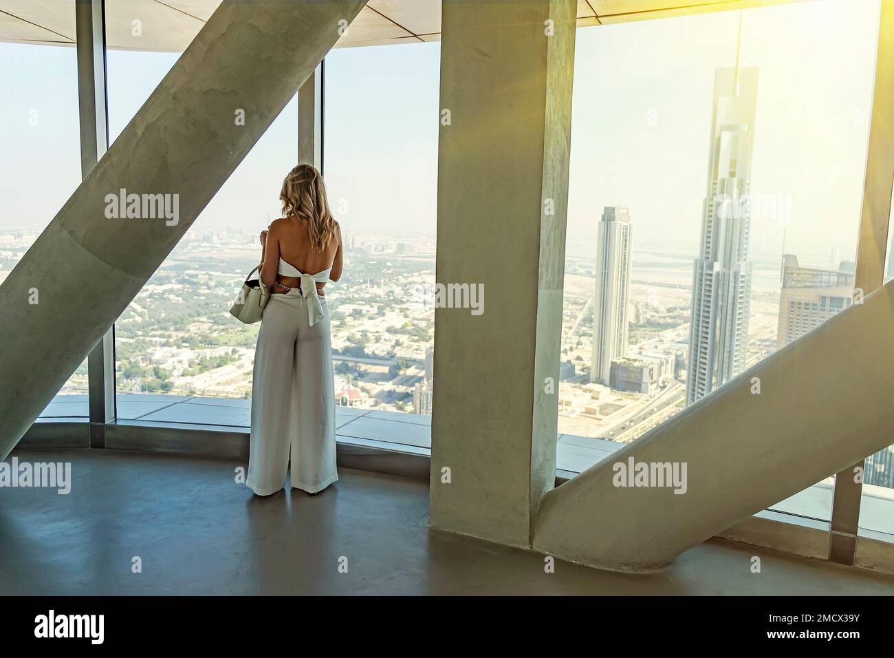 Young woman in modern high rise building with full length windows, Rear ...