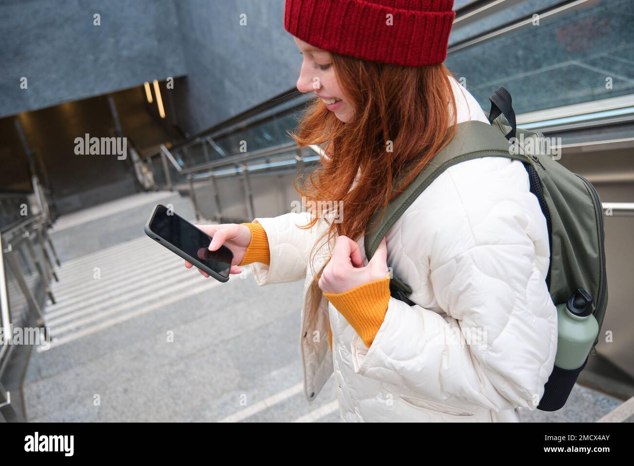 Smiling girl walking on stairs, using mobile phone, texting message on ...