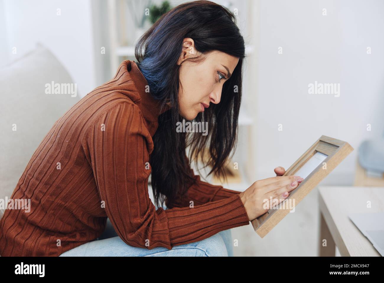 Woman looking sadly at the picture frames in her hands, crying over ...