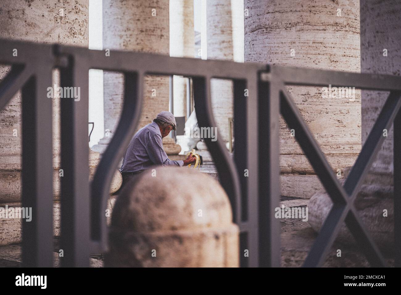 A senior man sitting and eating banana by the columns of old building ...