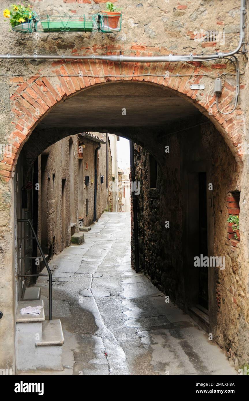 Red brick archway leading to a courtyard of houses, Roccatederighi ...