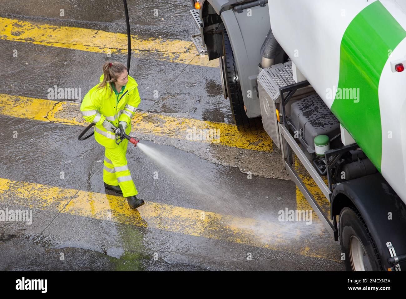 Woman worker cleaning a city road with high pressure water of a ...
