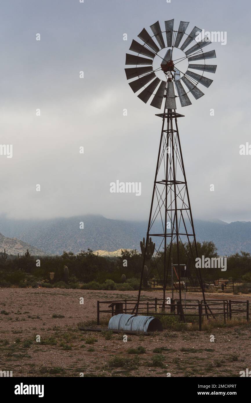 A vertical shot of windmill on rural ranch and farm next to forest ...