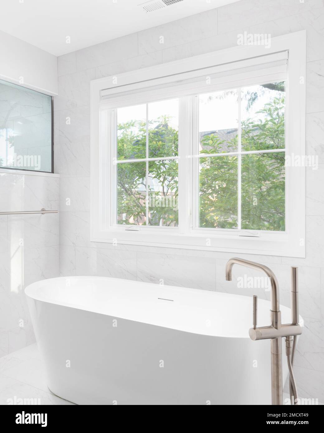 A white freestanding bathtub with a bronze faucet in front of a window ...