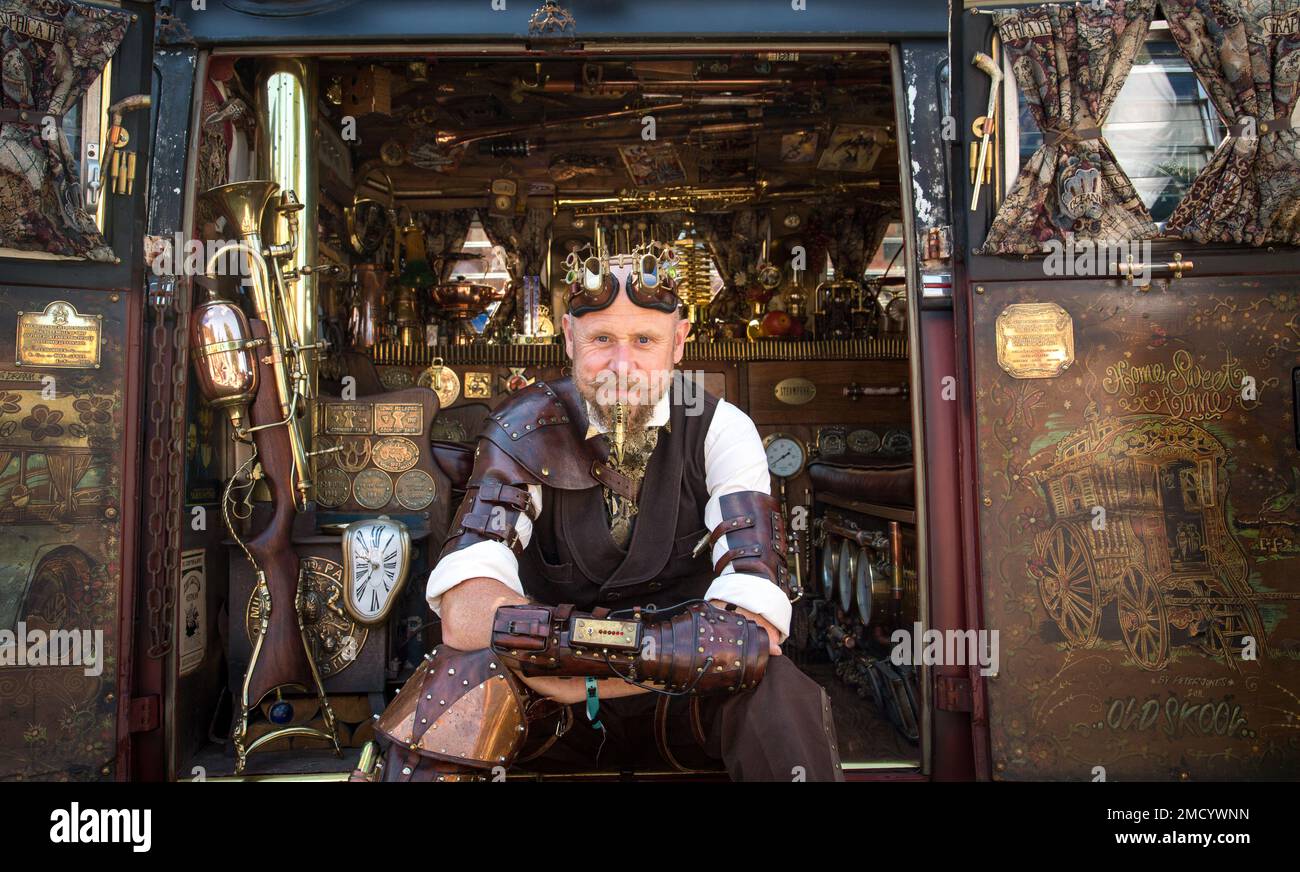 A steampunk sits on the side of his VW camper van showing its ...