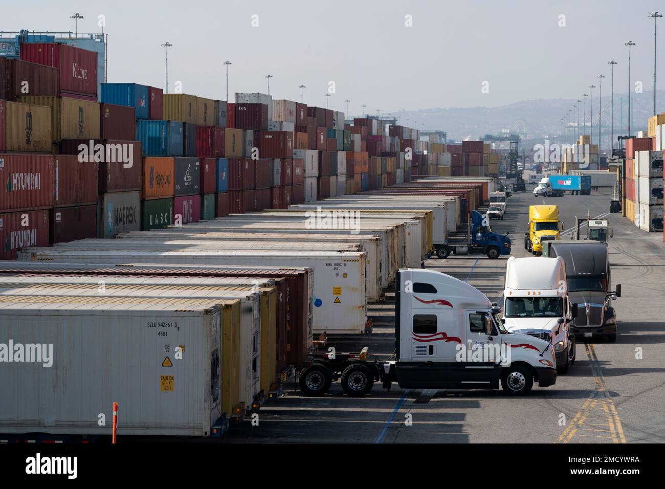 Trucks load and unload shipping containers at the Port of Long Beach in ...