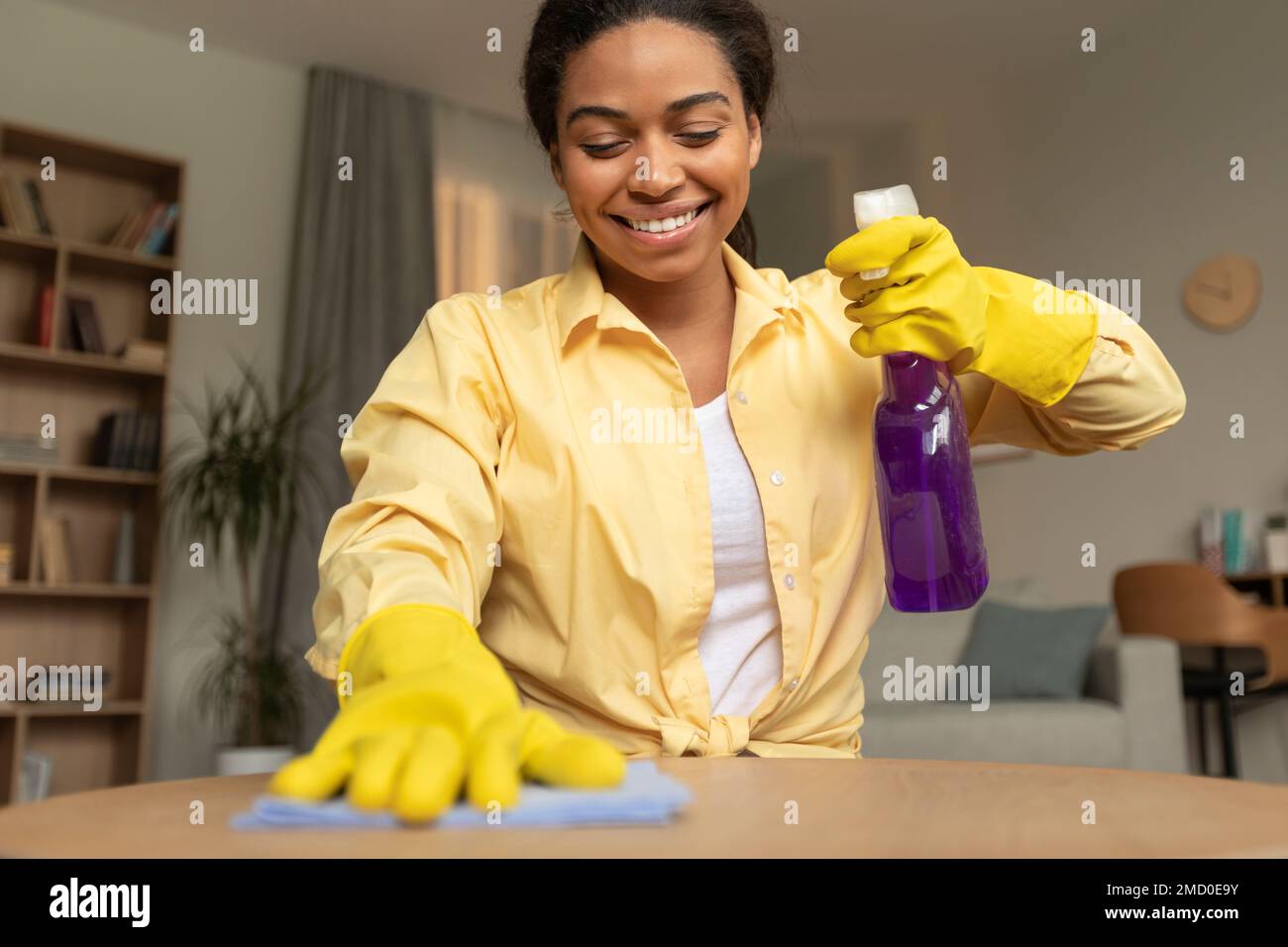 Cheerful african american woman in rubber gloves cleaning table in ...