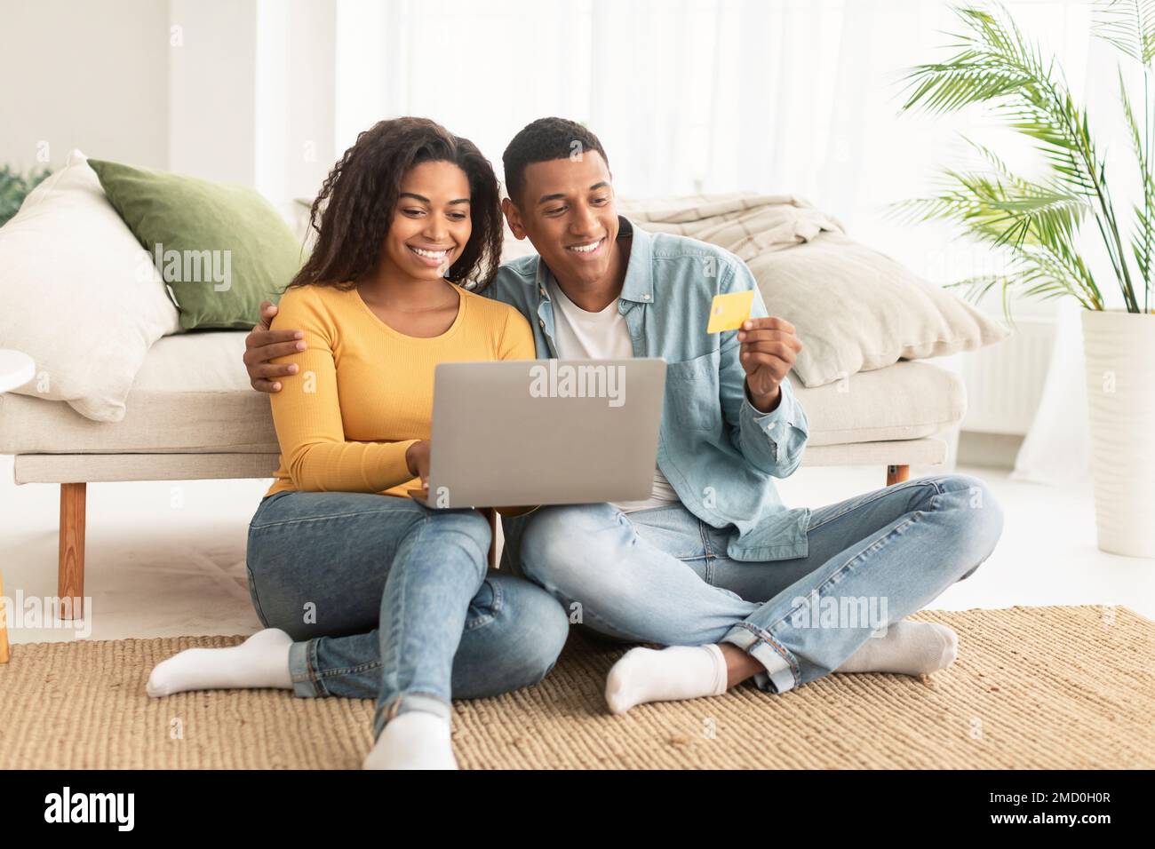 Smiling young african american male and female hug, using credit card ...