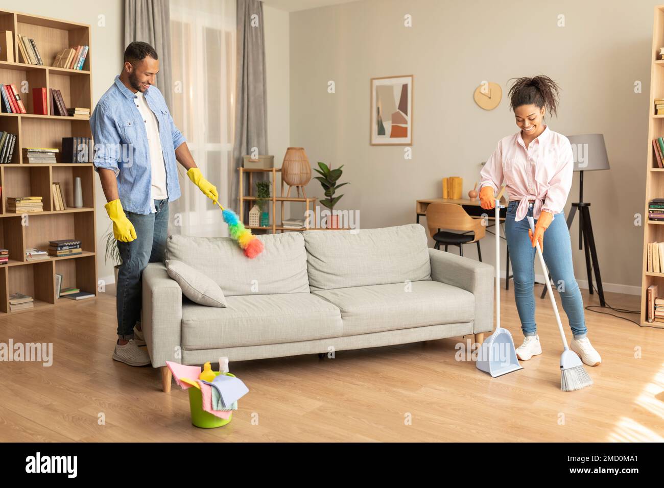 Shared house cleaning. Black man in rubber gloves and duster wiping ...