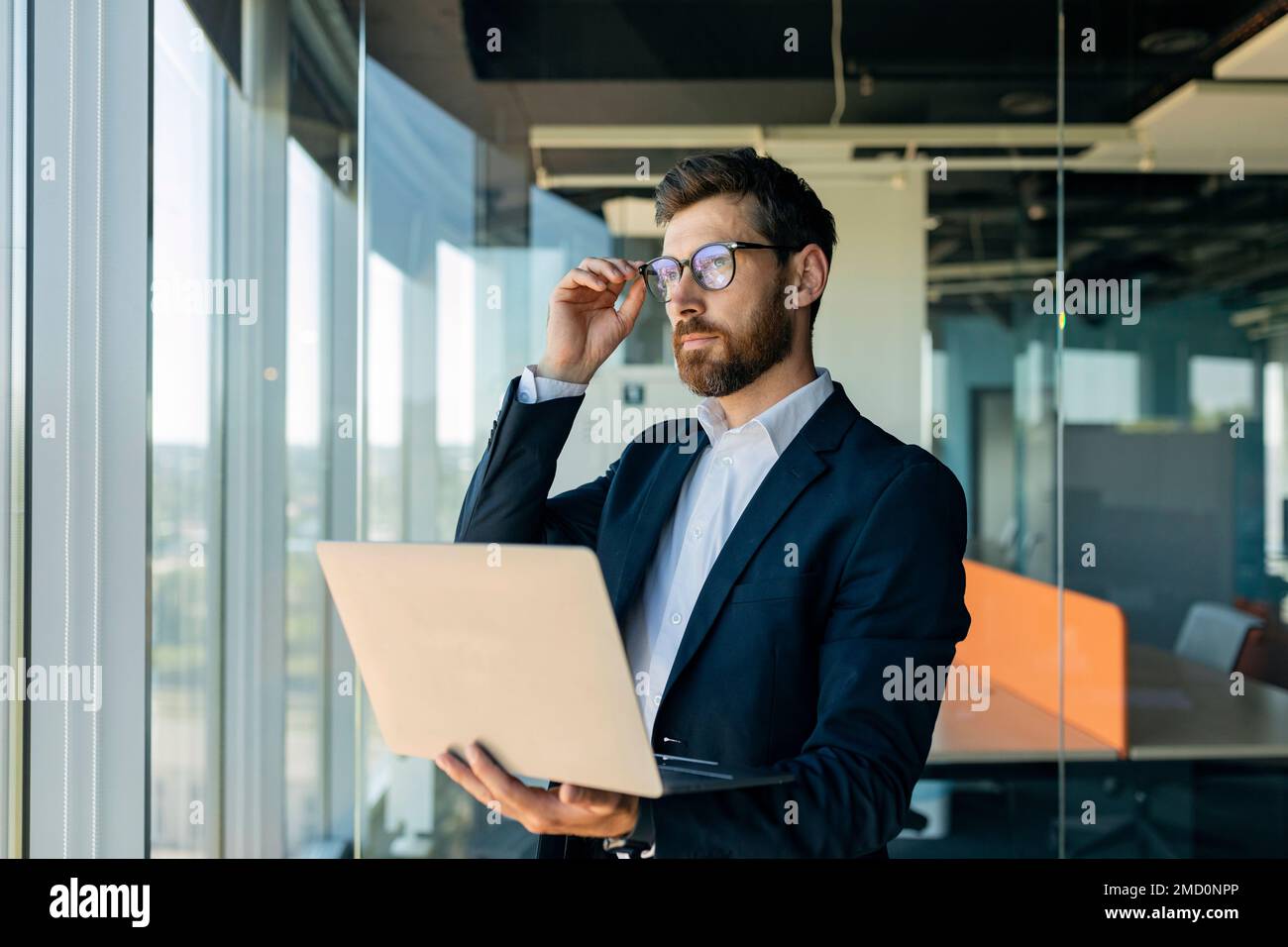 Serious middle aged businessman in glasses holding laptop and looking ...