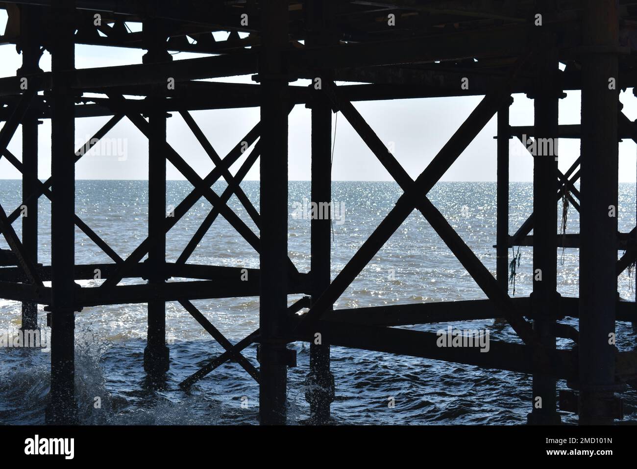 The wooden Blackpool Pier legs black on the Irish Sea water with blue ...