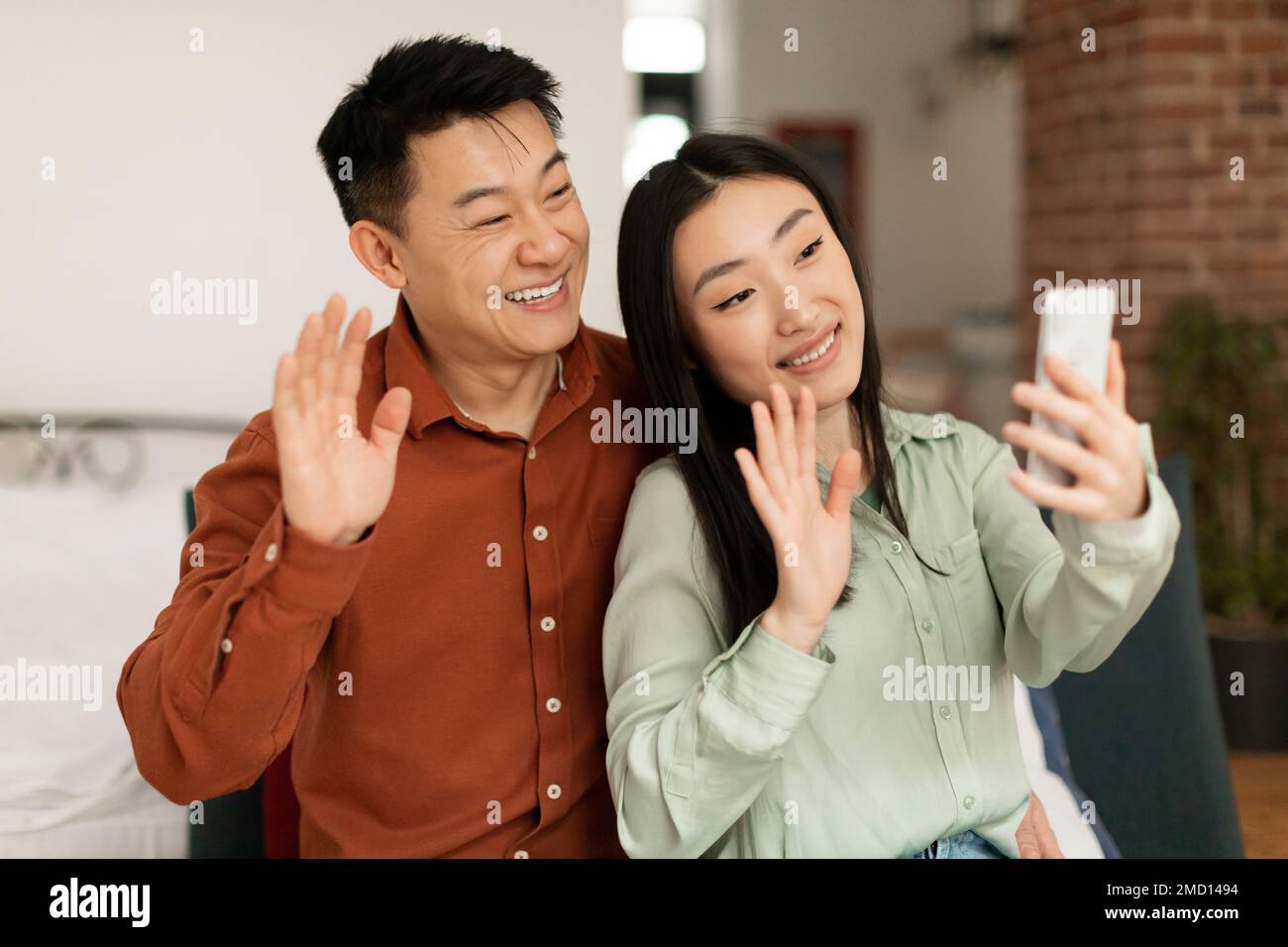Remote communication. Happy asian spouses waving at smartphone ...