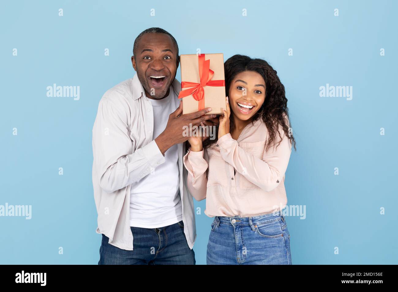 Excited african american couple holding wrapped gift box, listening to ...