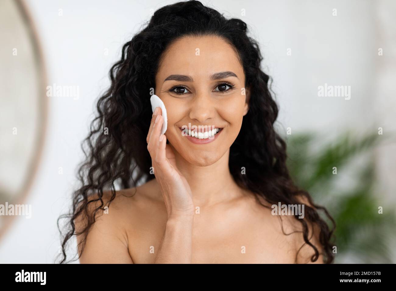 Portrait of happy arabic millennial curly female cleaning skin with ...