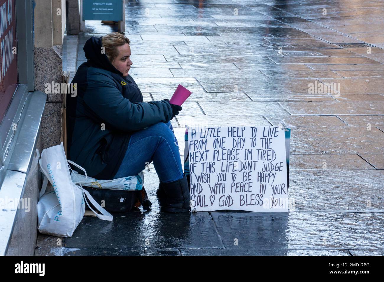 Young woman sitting on some carrier bags, begging with a sign, Argyll ...