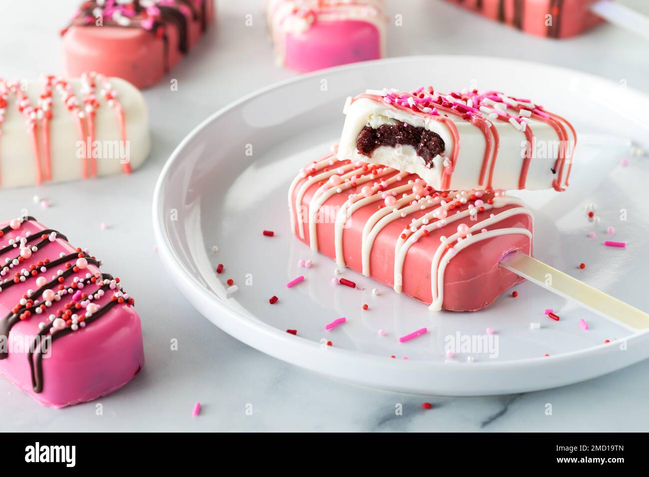 Valentine's Day cakesicles on a plate with sprinkles with a bite out of ...